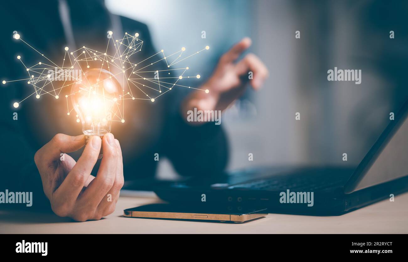 Businessman hand holding light bulb with icons and working on the desk ...