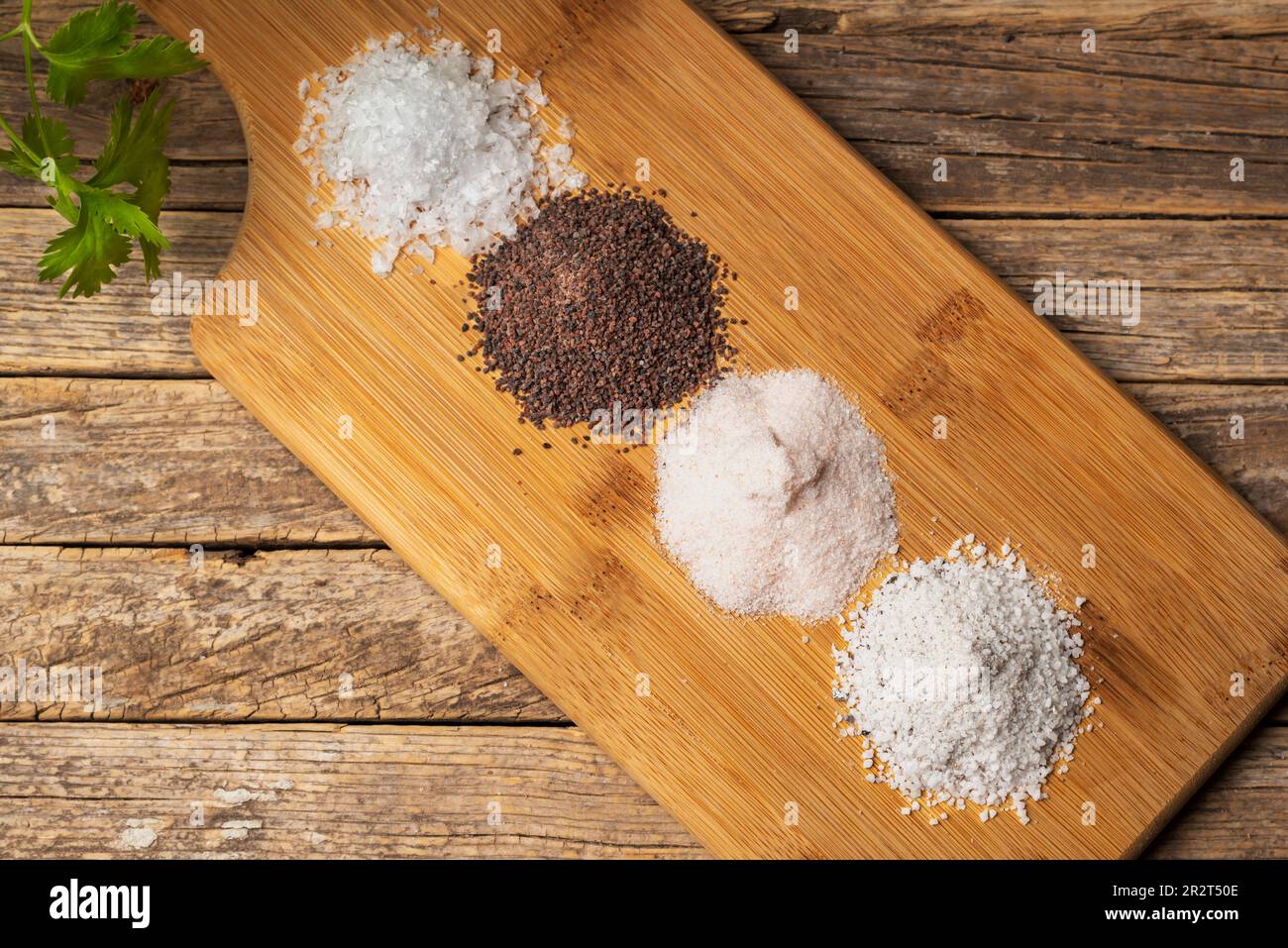 Wooden table with piles of different types of salt, black, pink, flake ...