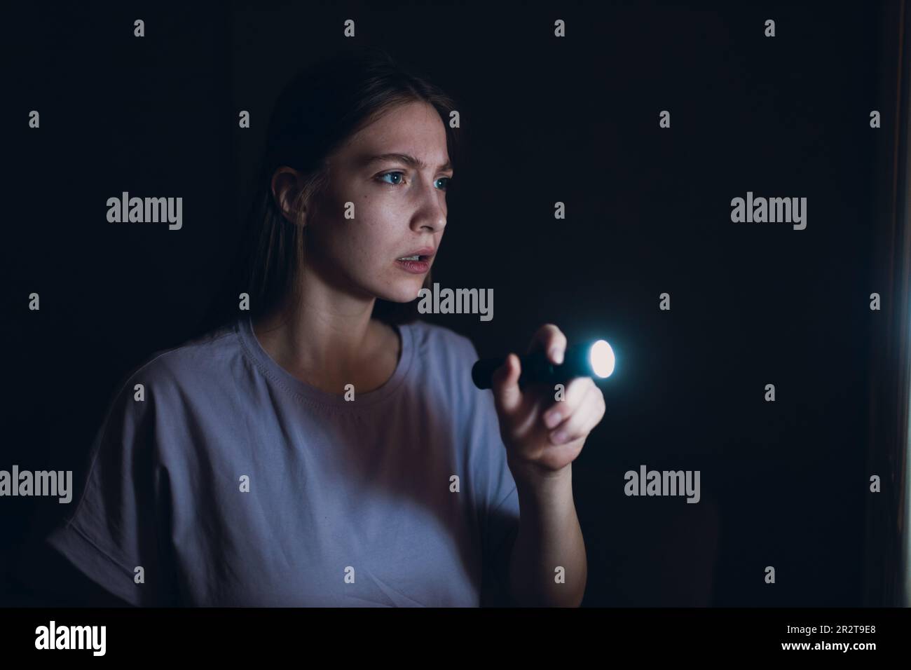 Woman scared holding hand flashlight in darkness and afraid of violence ...