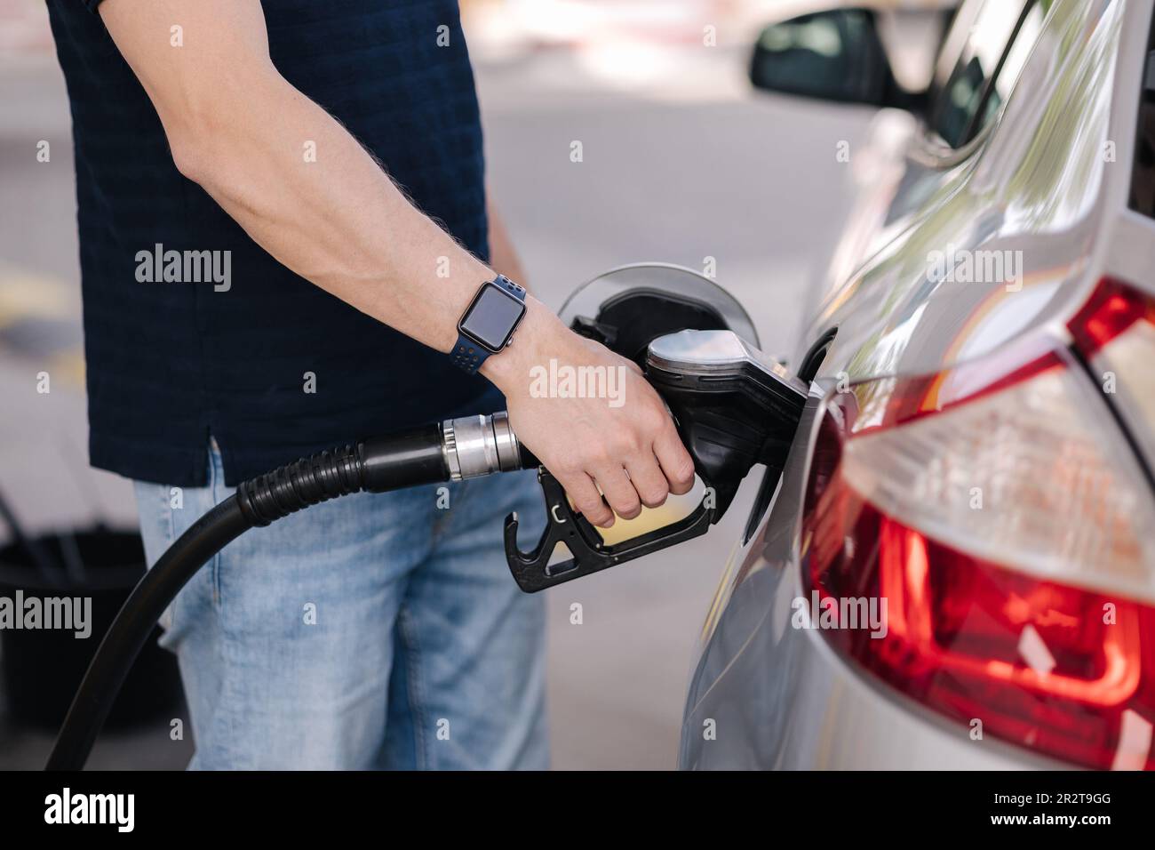Close-up of young man refuelling a car at a petrol station. Middle ...
