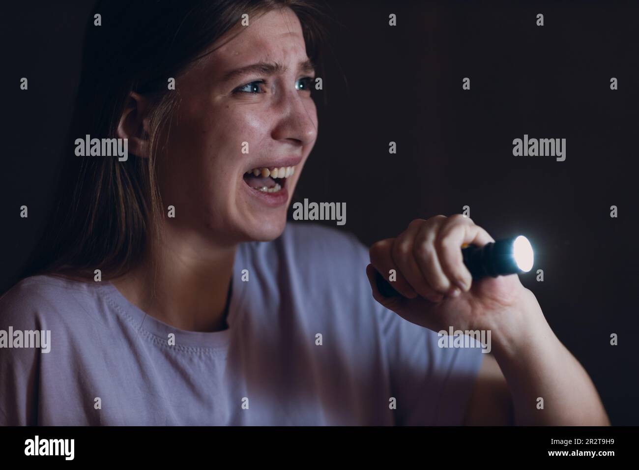Woman scared holding hand flashlight in darkness and afraid of violence ...