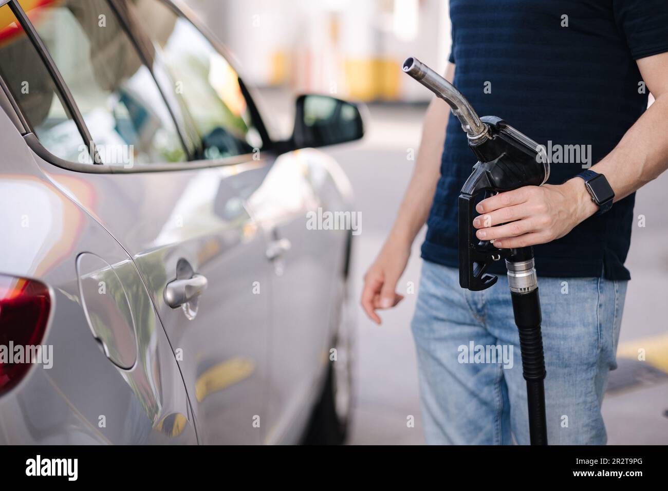 Close-up of young man refuelling a car at a petrol station. Middle ...