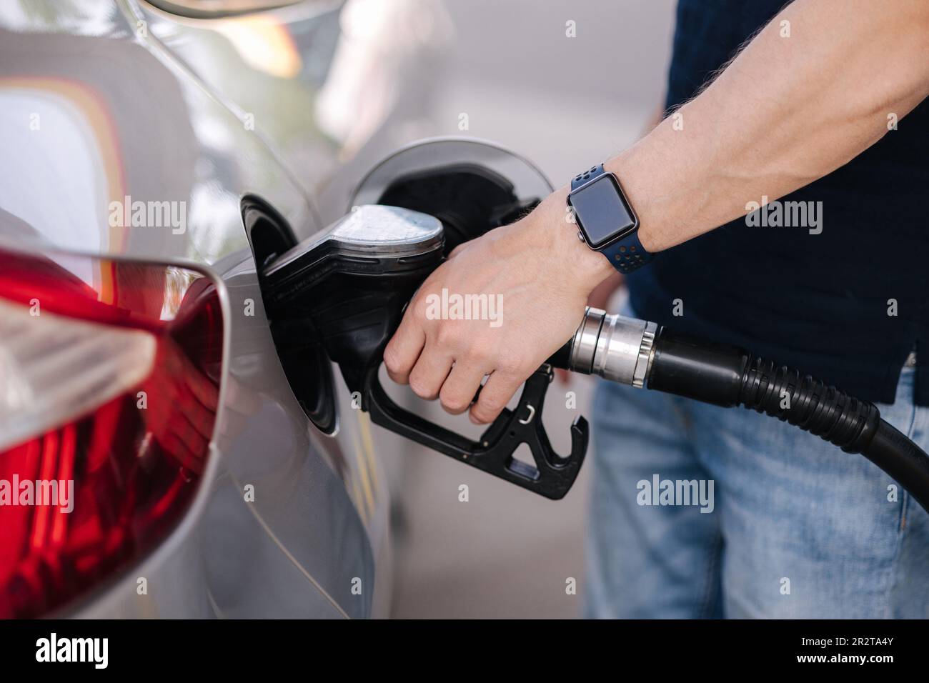 Close-up of young man refuelling a car at a petrol station. Middle ...