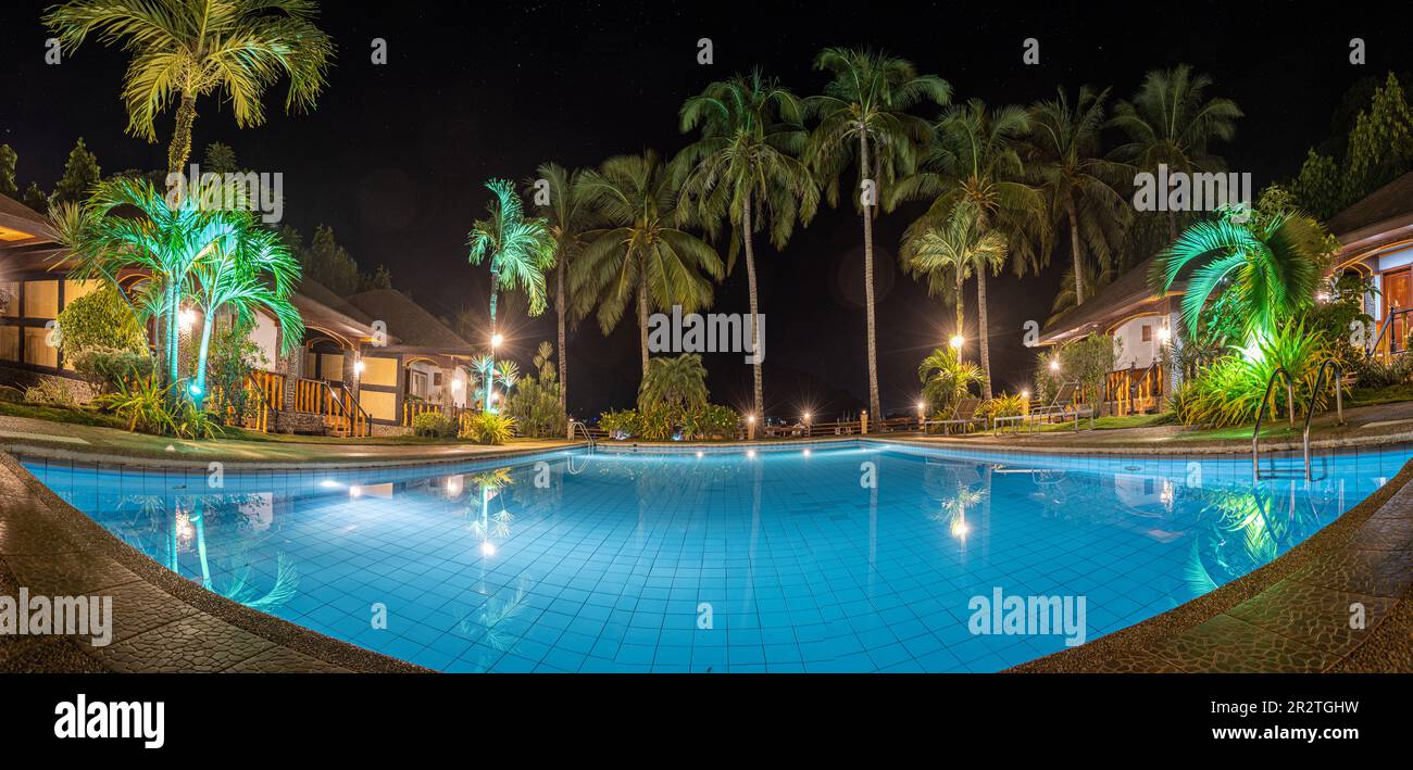 Night shot over illuminated swimming pool in tropical environment with ...