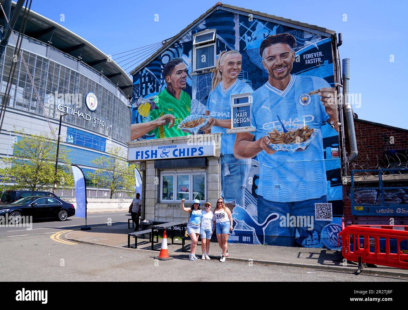Manchester City fans pose for a photo in front of a mural on the side ...