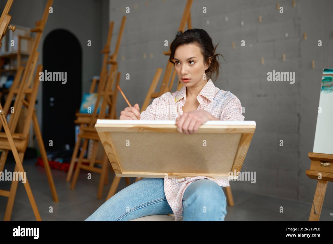 Attractive young woman artist holding canvas in hand drawing picture ...