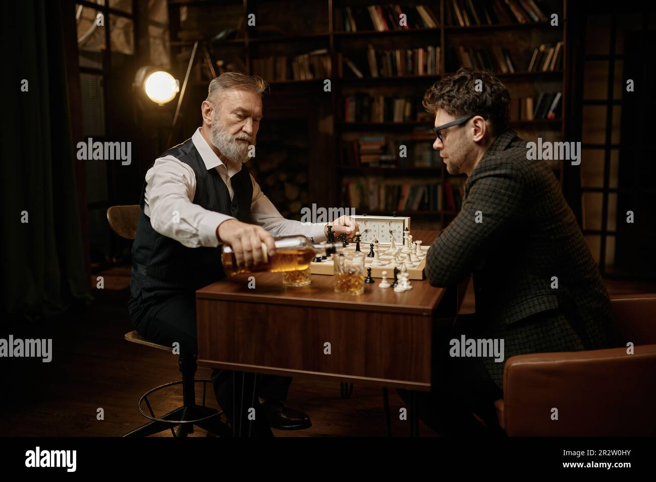 Elderly father and millennial son playing chess and drinking whisky ...
