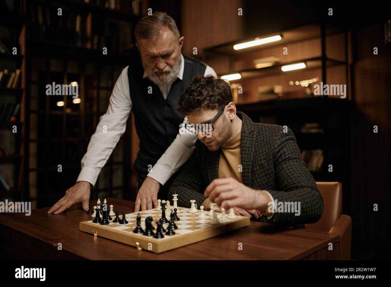 Senior man teaching young guy playing chess explaining rules of game ...