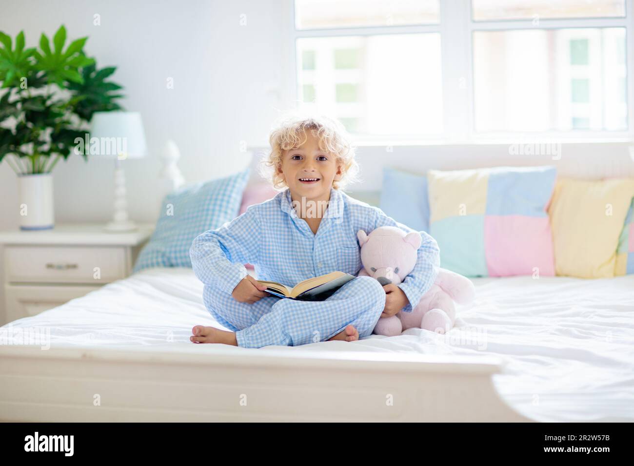 Child reading book in bed in white sunny bedroom with window. Children ...