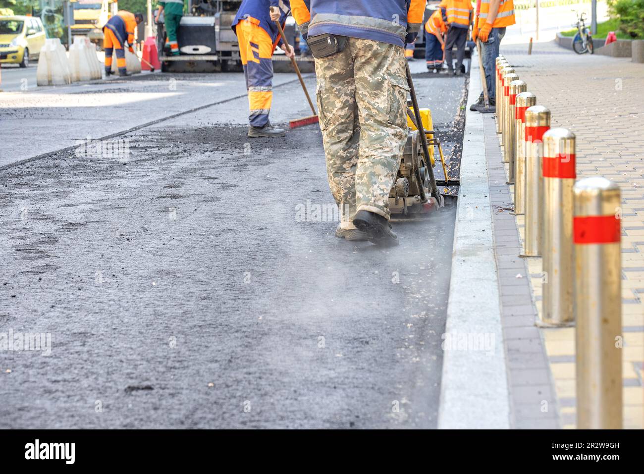 Workers lay a layer of asphalt along a paved sidewalk for the final ...