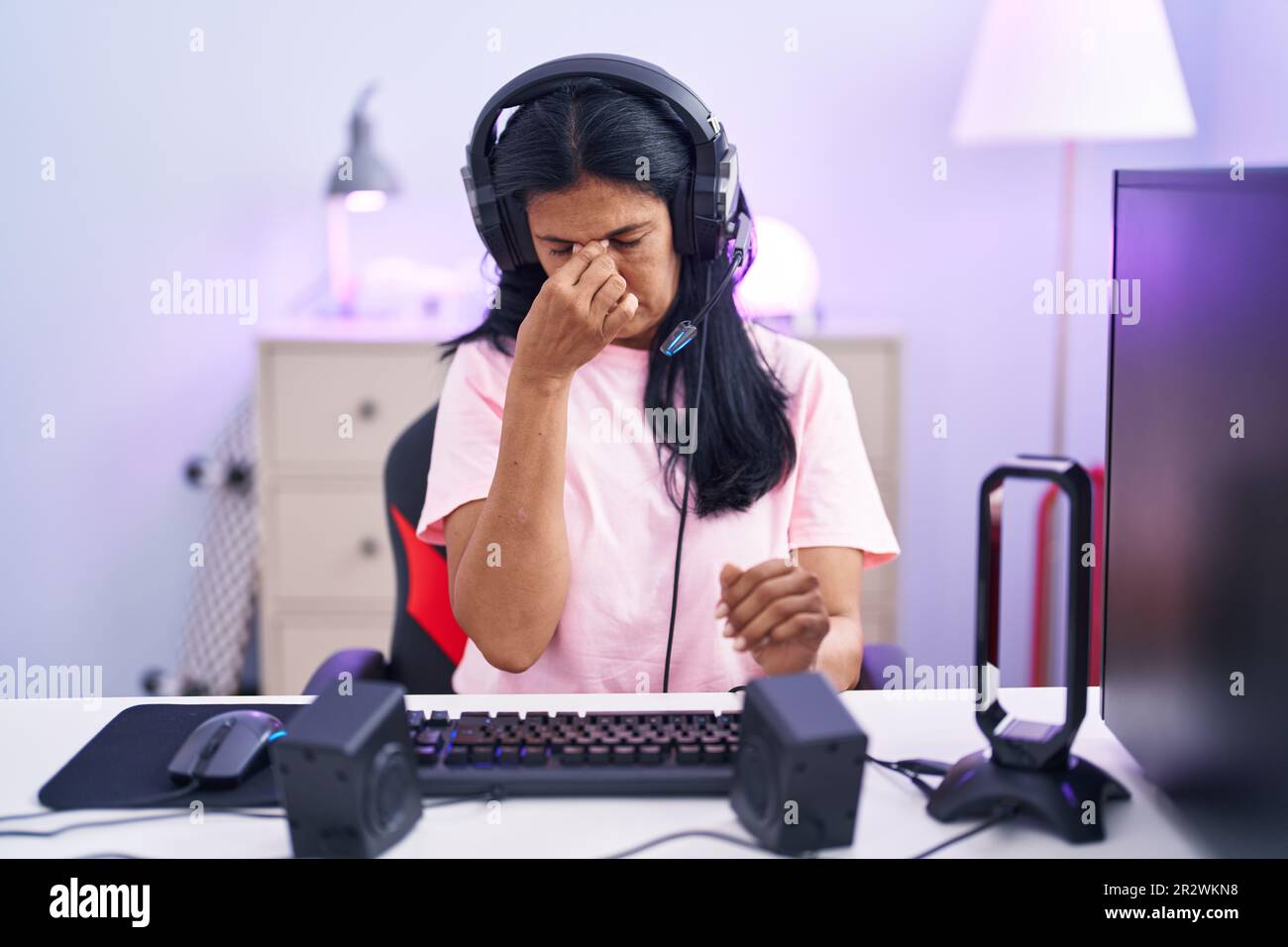 Mature hispanic woman playing video games at home tired rubbing nose ...
