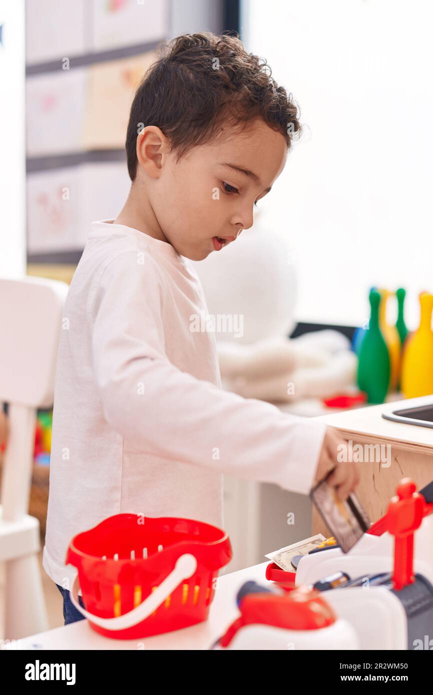 Adorable hispanic boy playing supermarket game standing at kindergarten ...