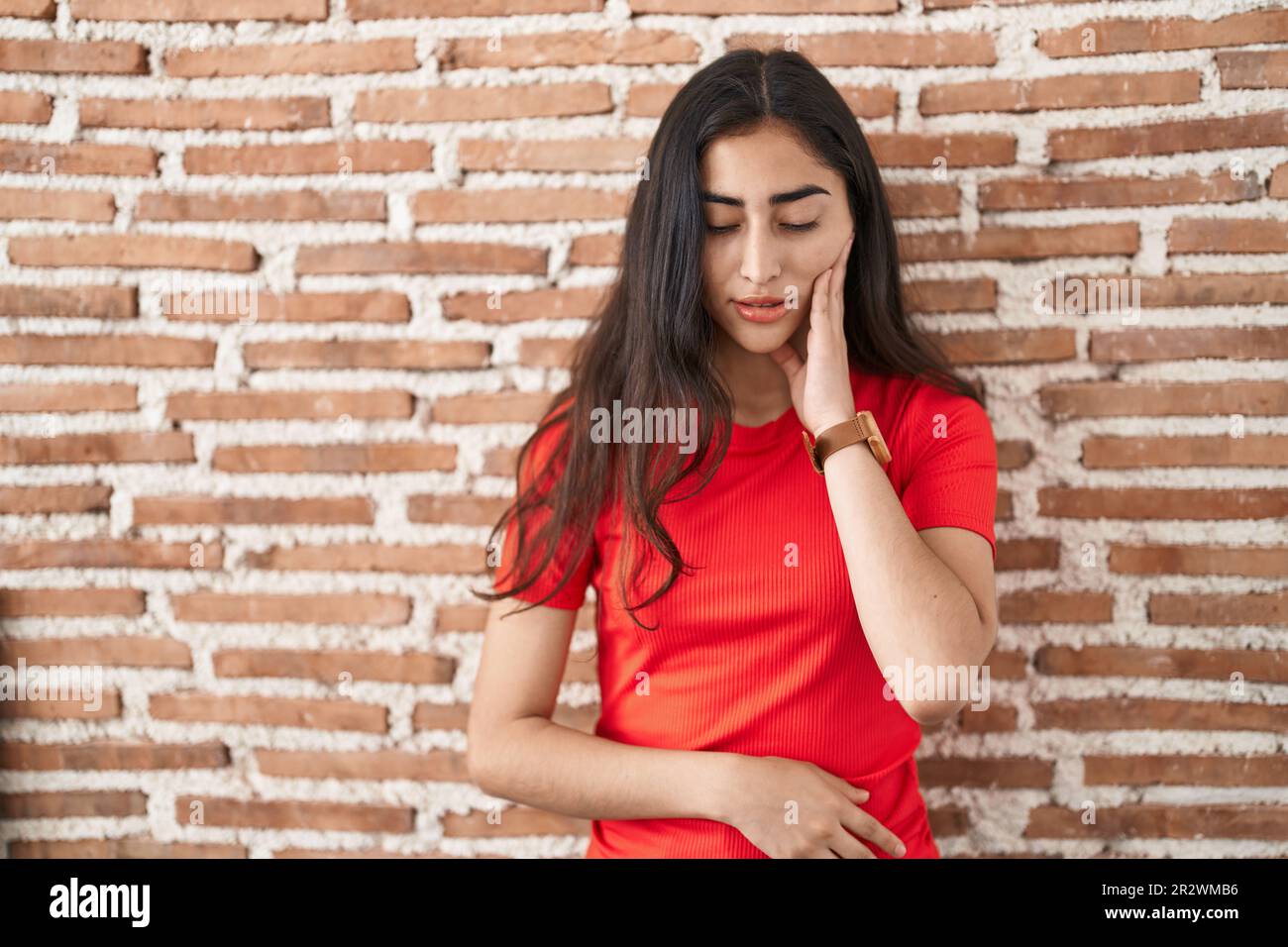 Young teenager girl standing over bricks wall touching mouth with hand ...