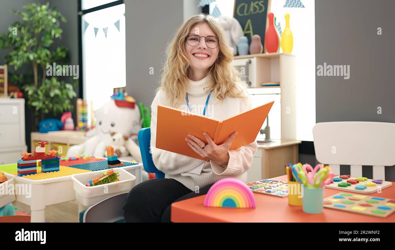 Young blonde woman preschool teacher reading book with relaxed ...