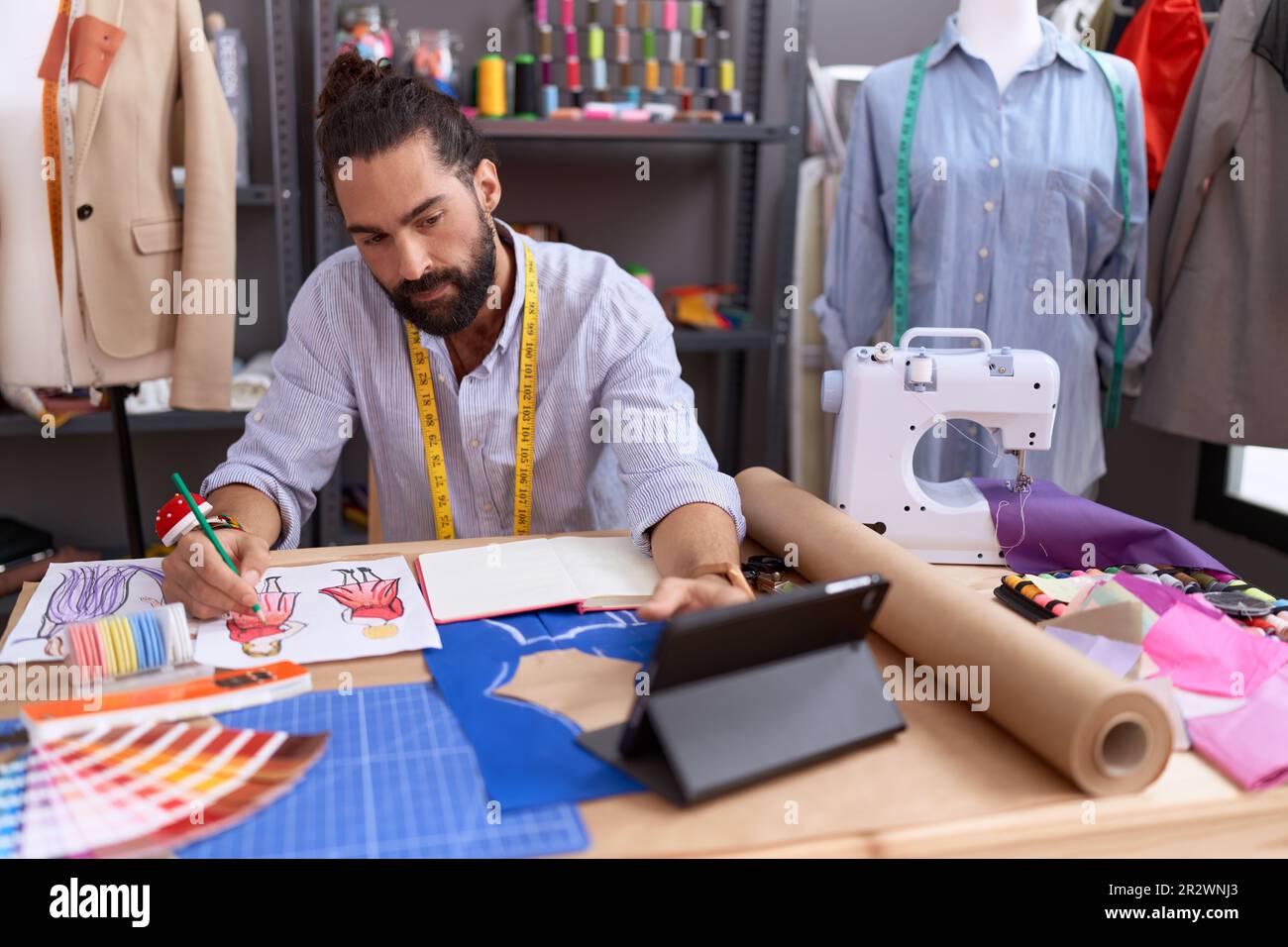 Young hispanic man tailor drawing clothing design using touchpad at ...