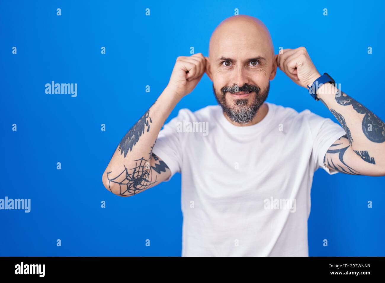 Hispanic man with tattoos standing over blue background smiling pulling ...
