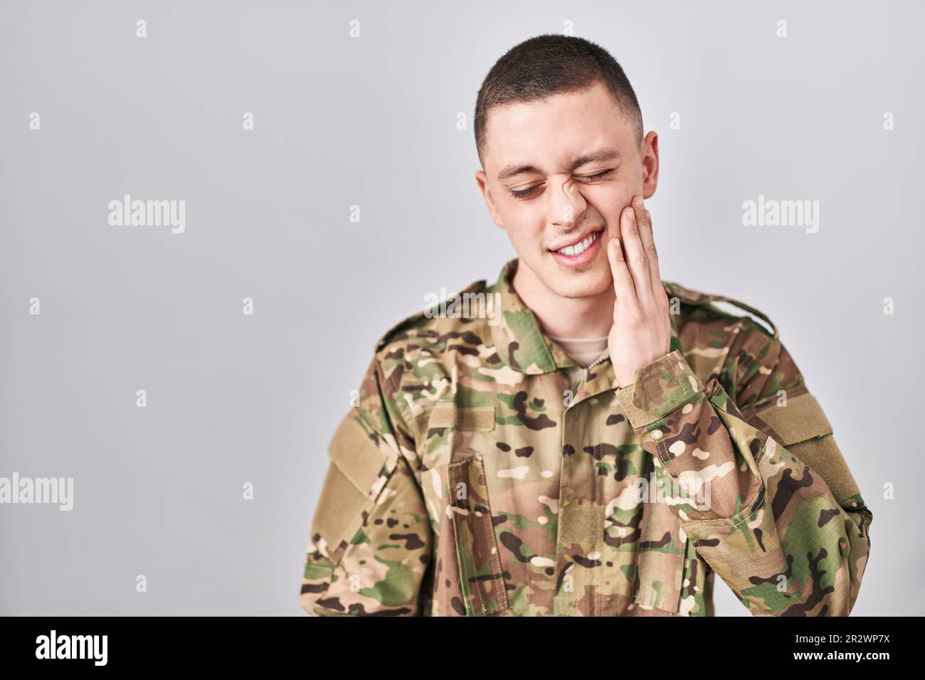 Young man wearing camouflage army uniform touching mouth with hand with ...