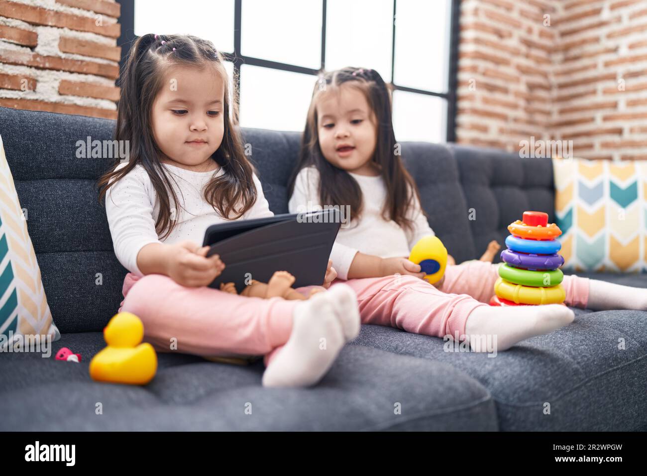Adorable twin girls playing with hoops game using touchpad at home ...