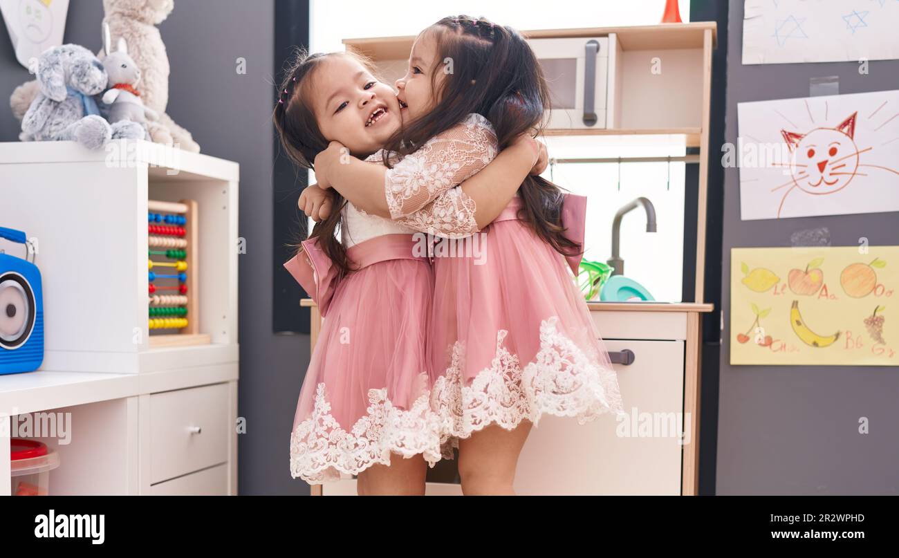 Adorable twin girls playing with play kitchen hugging each other at ...