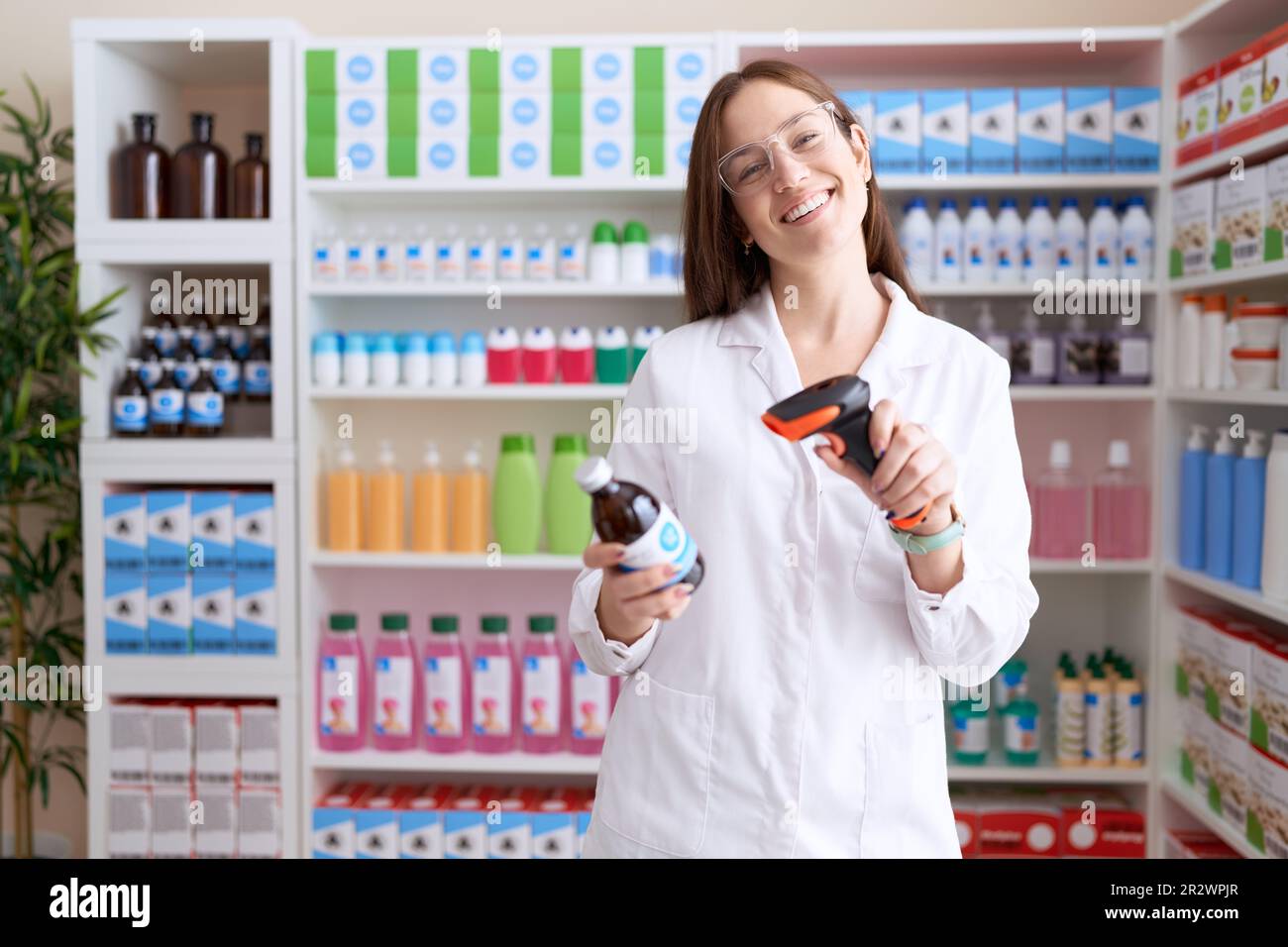 Young beautiful woman pharmacist scanning medication bottle at pharmacy ...