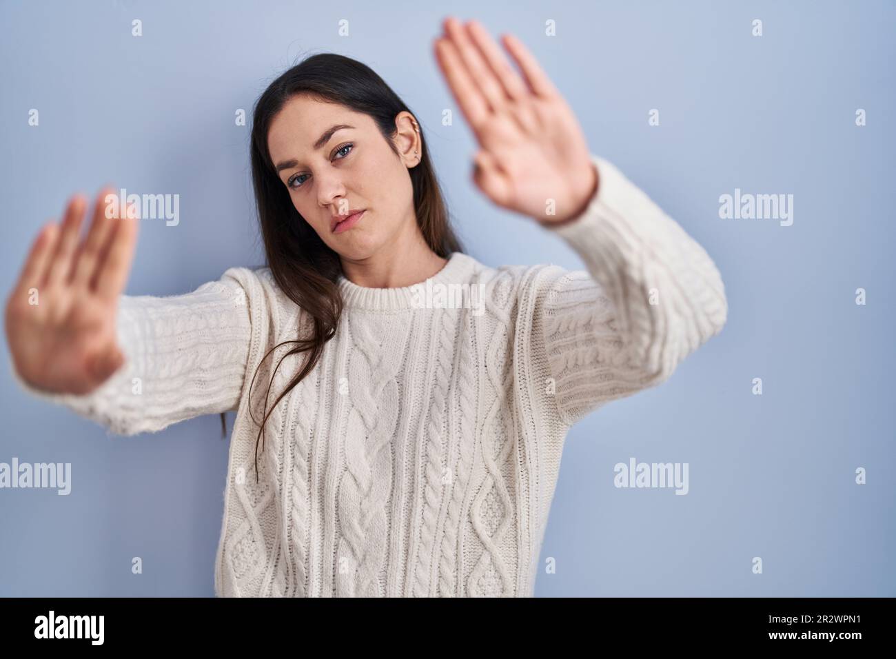 Young brunette woman standing over blue background doing frame using ...