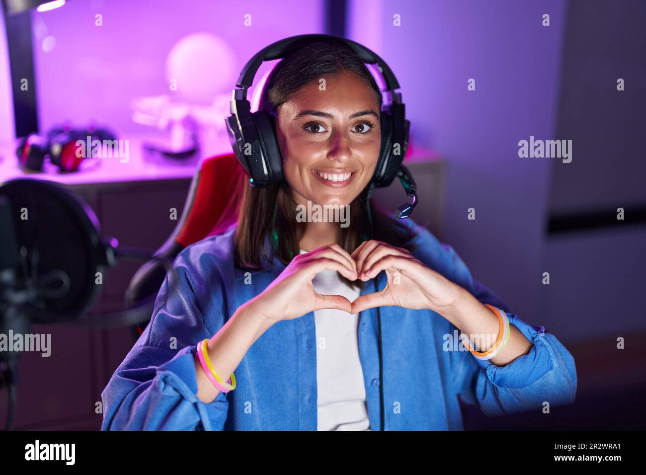 Young beautiful hispanic woman streamer smiling confident doing heart ...