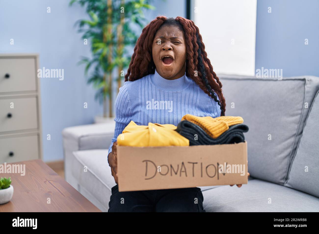 African woman holding donations box for charity angry and mad screaming ...