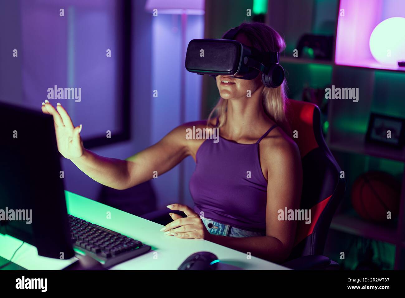 Young blonde woman streamer playing video game using virtual reality ...