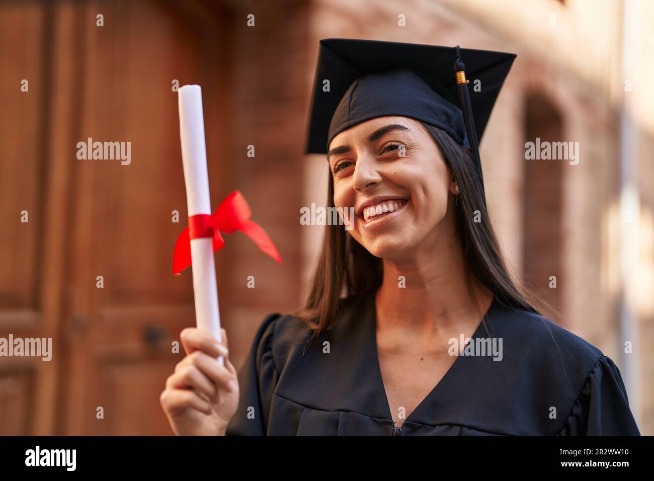 Young hispanic woman wearing graduated uniform holding diploma at ...