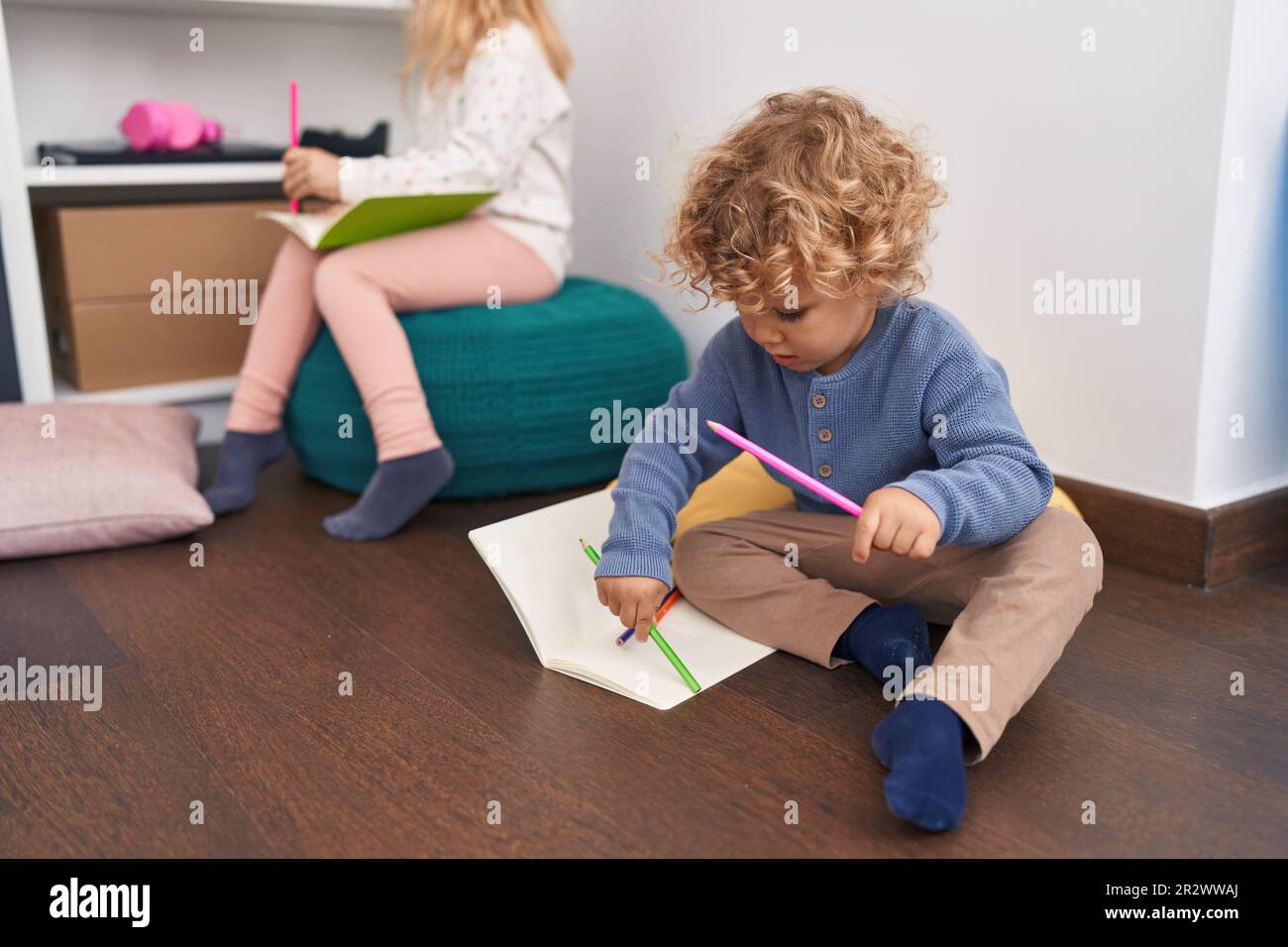 Adorable boy and girl students sitting on floor drawing on notebook at ...