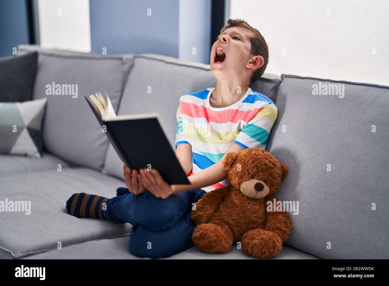 Young caucasian kid sitting on the sofa reading a book angry and mad ...