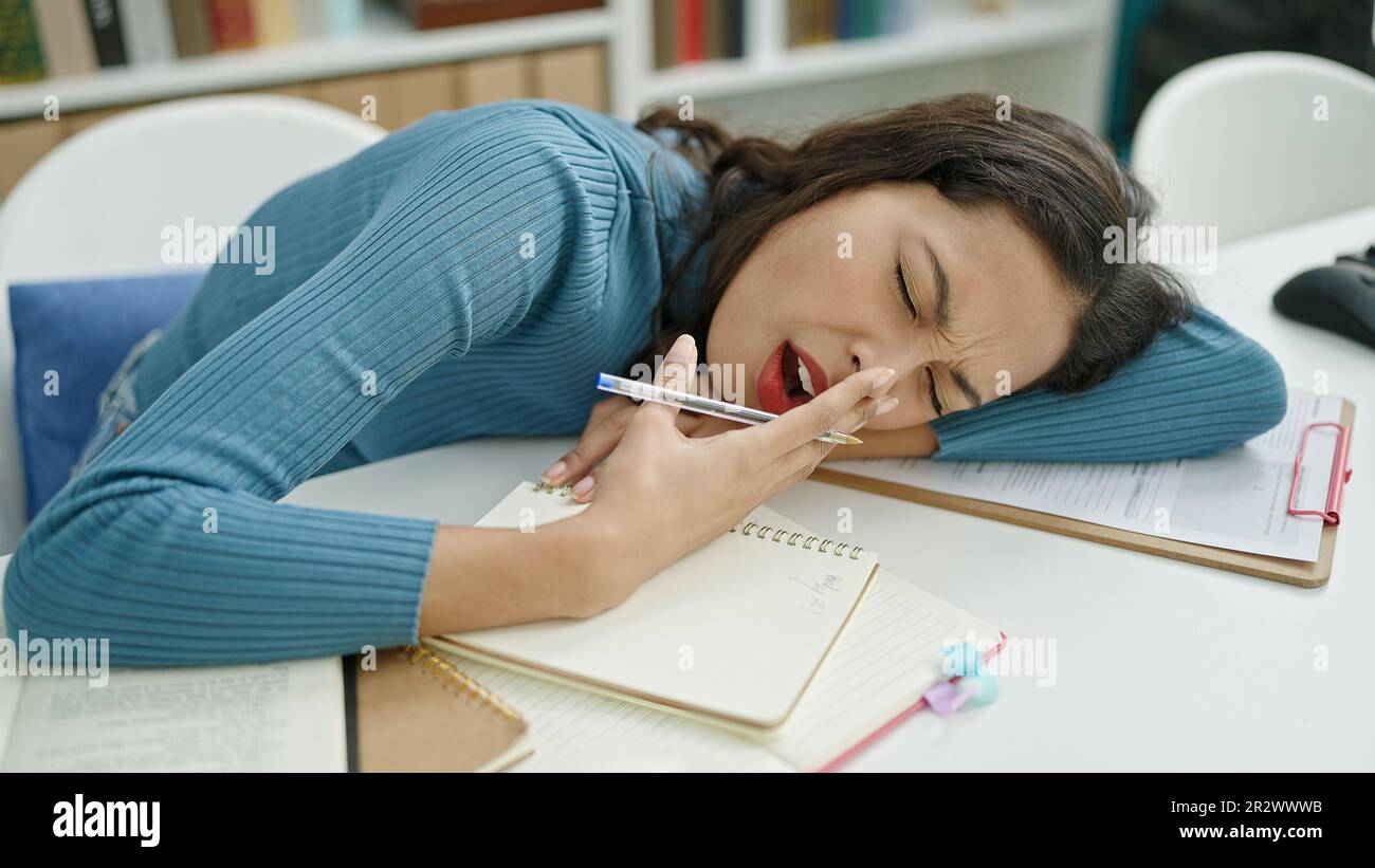 Young beautiful hispanic woman student writing notes tired at ...