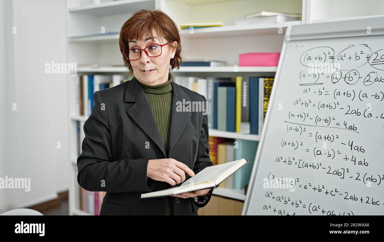 Mature hispanic woman teacher standing reading book at library university Stock Photo - Alamy