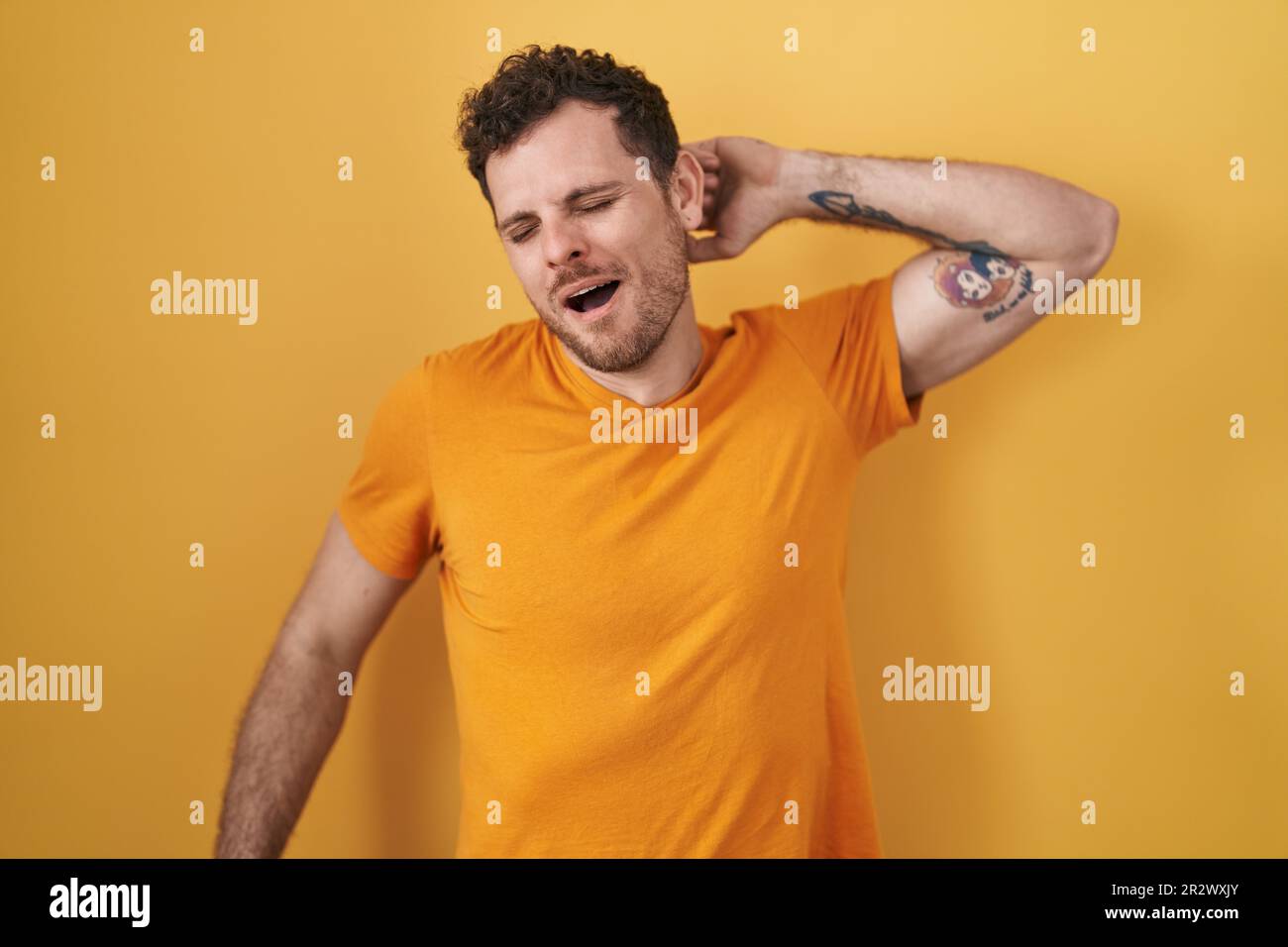 Young hispanic man standing over yellow background stretching back ...