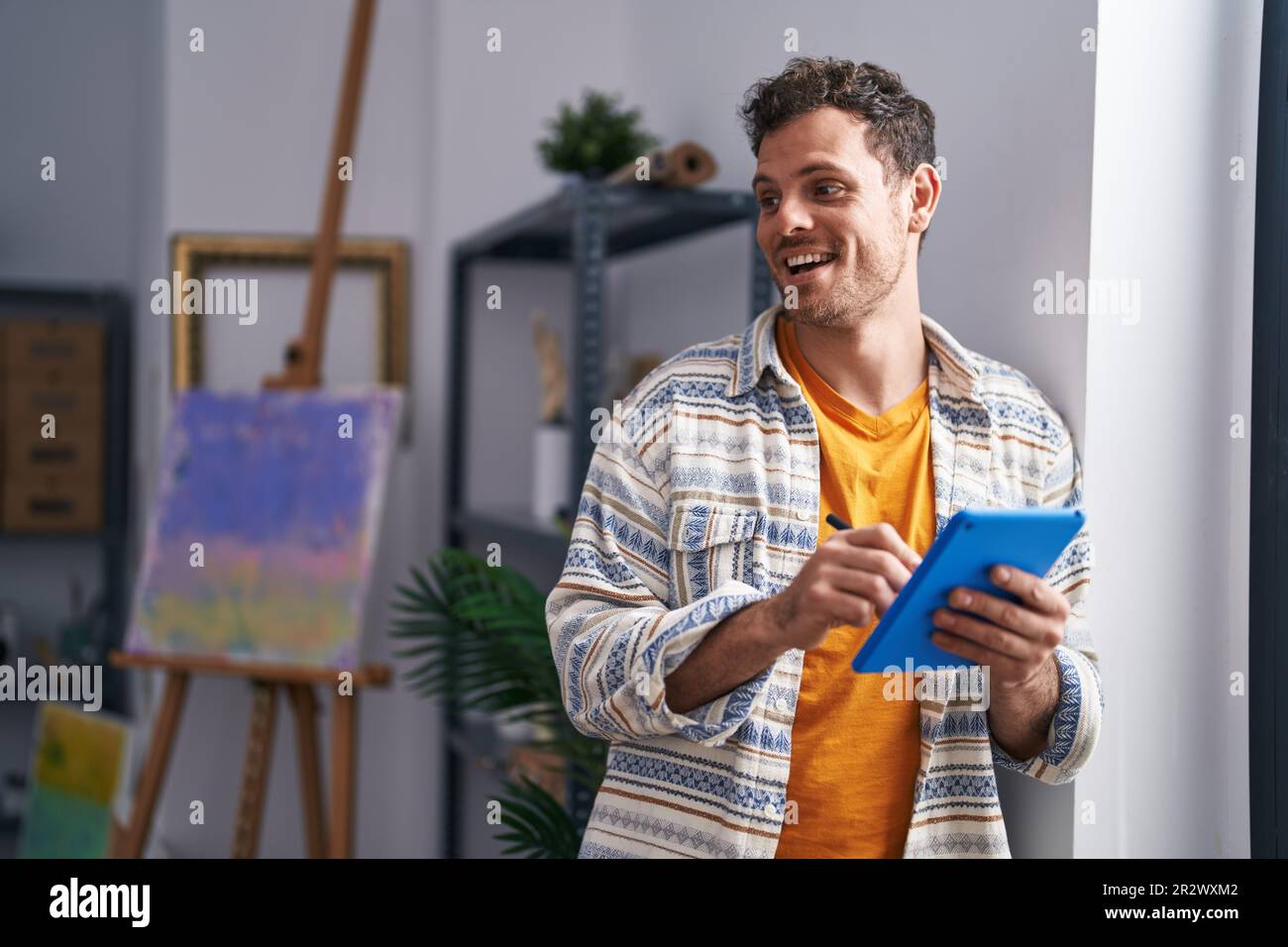 Young hispanic man artist using touchpad standing at art studio Stock ...