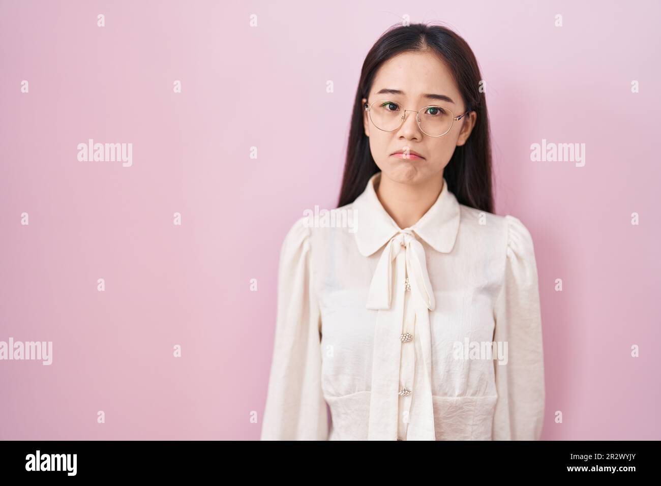 Young chinese woman standing over pink background depressed and worry ...