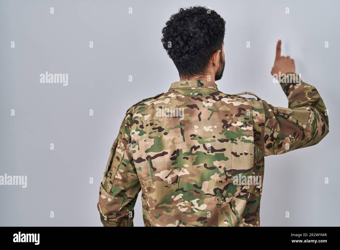 Arab man wearing camouflage army uniform posing backwards pointing ...