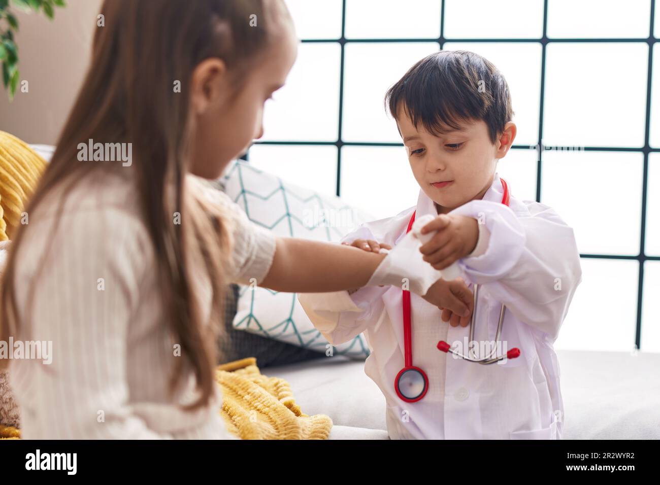 Adorable boy and girl wearing doctor uniform bandaging arm at home ...