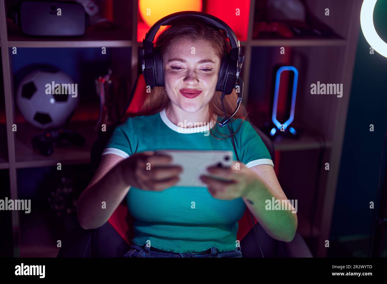 Young redhead woman streamer playing video game using smartphone at ...