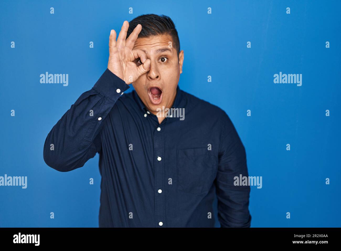 Hispanic young man standing over blue background doing ok gesture ...