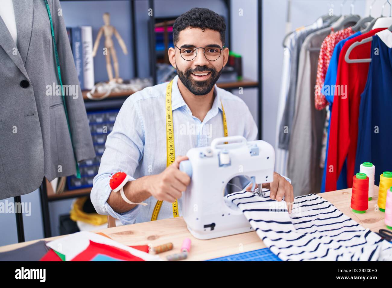 Young arab man tailor smiling confident using sewing machine at tailor ...