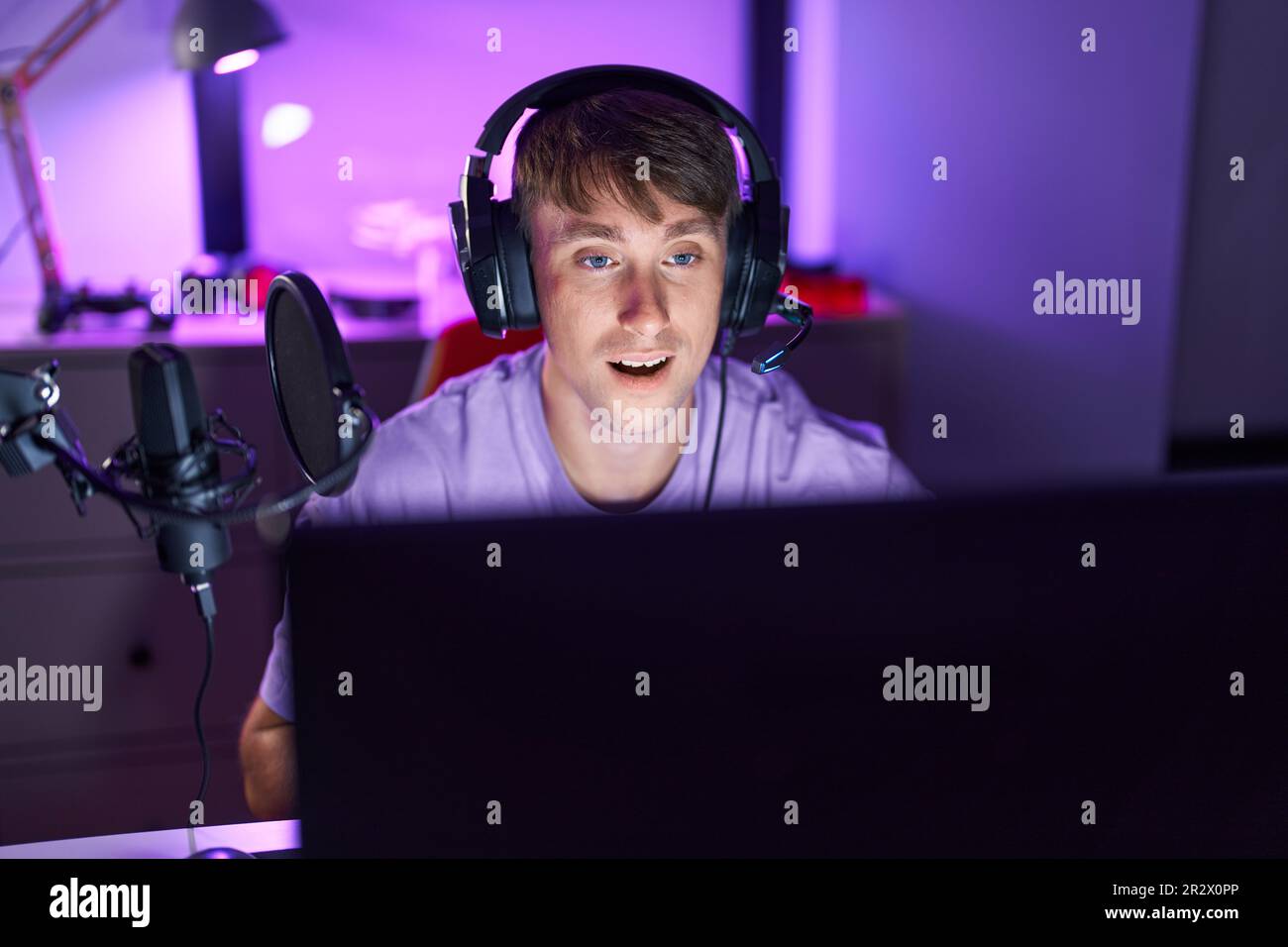 Caucasian blond man playing video games scared and amazed with open ...