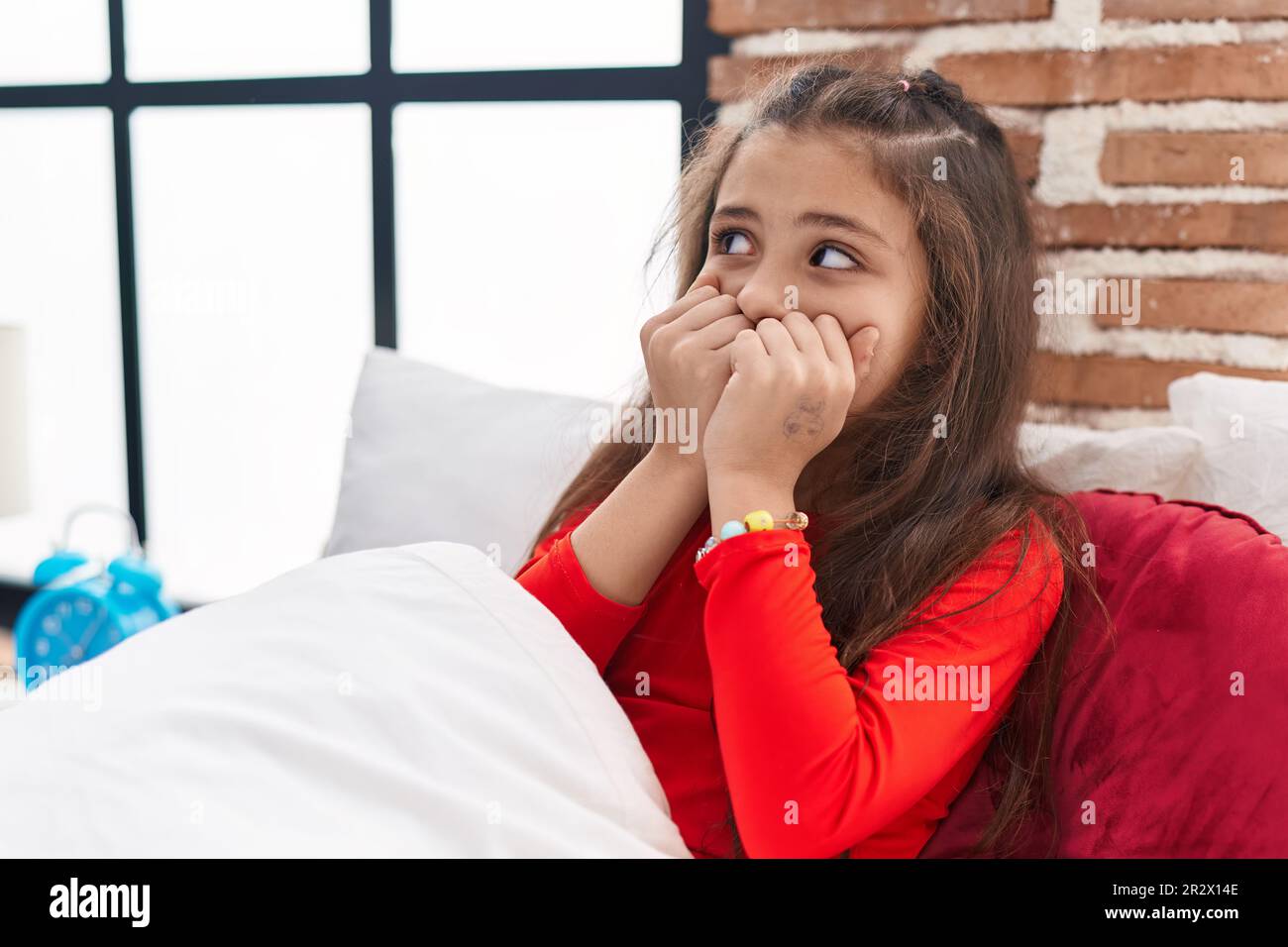 Adorable hispanic girl sitting on the bed with fear expression at ...