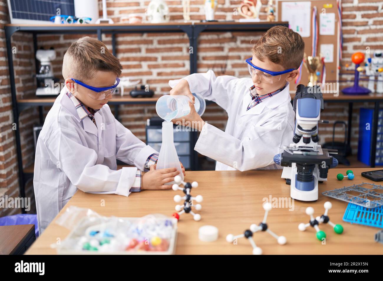 Adorable boys student pouring liquid on test tube at laboratory ...
