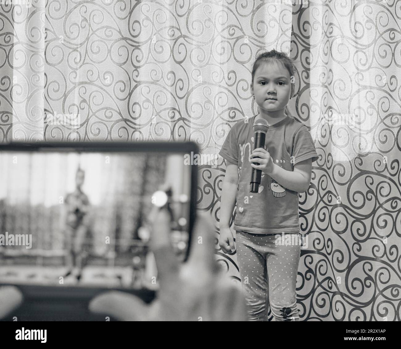 Cute little Asian girl looking at camera holding microphone at home ...
