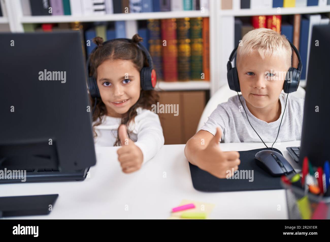 Adorable boy and girl students using computer and headphones doing ...