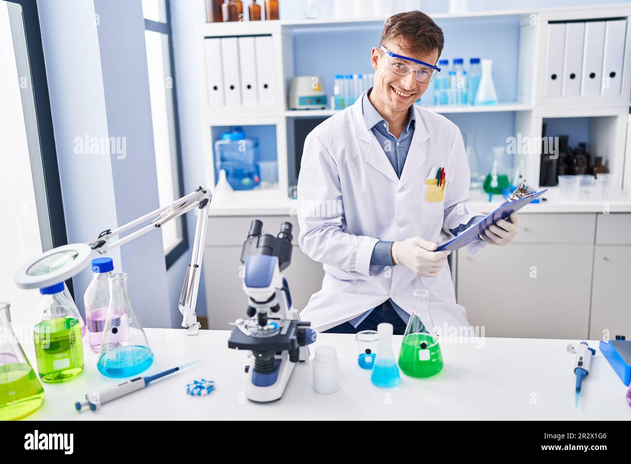 Young man scientist smiling confident reading report at laboratory Stock Photo - Alamy