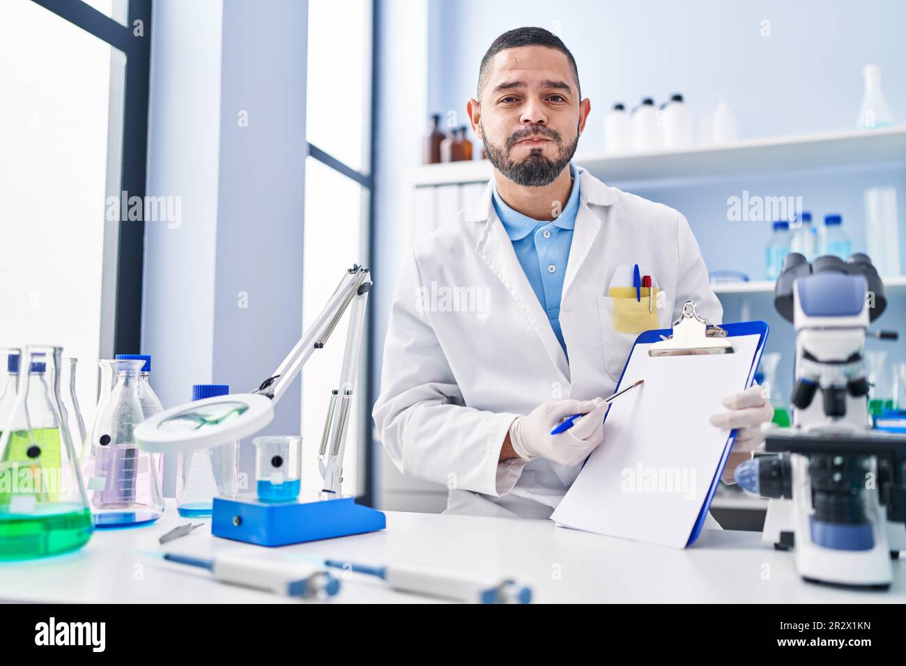 Hispanic man working at scientist laboratory holding blank clipboard ...