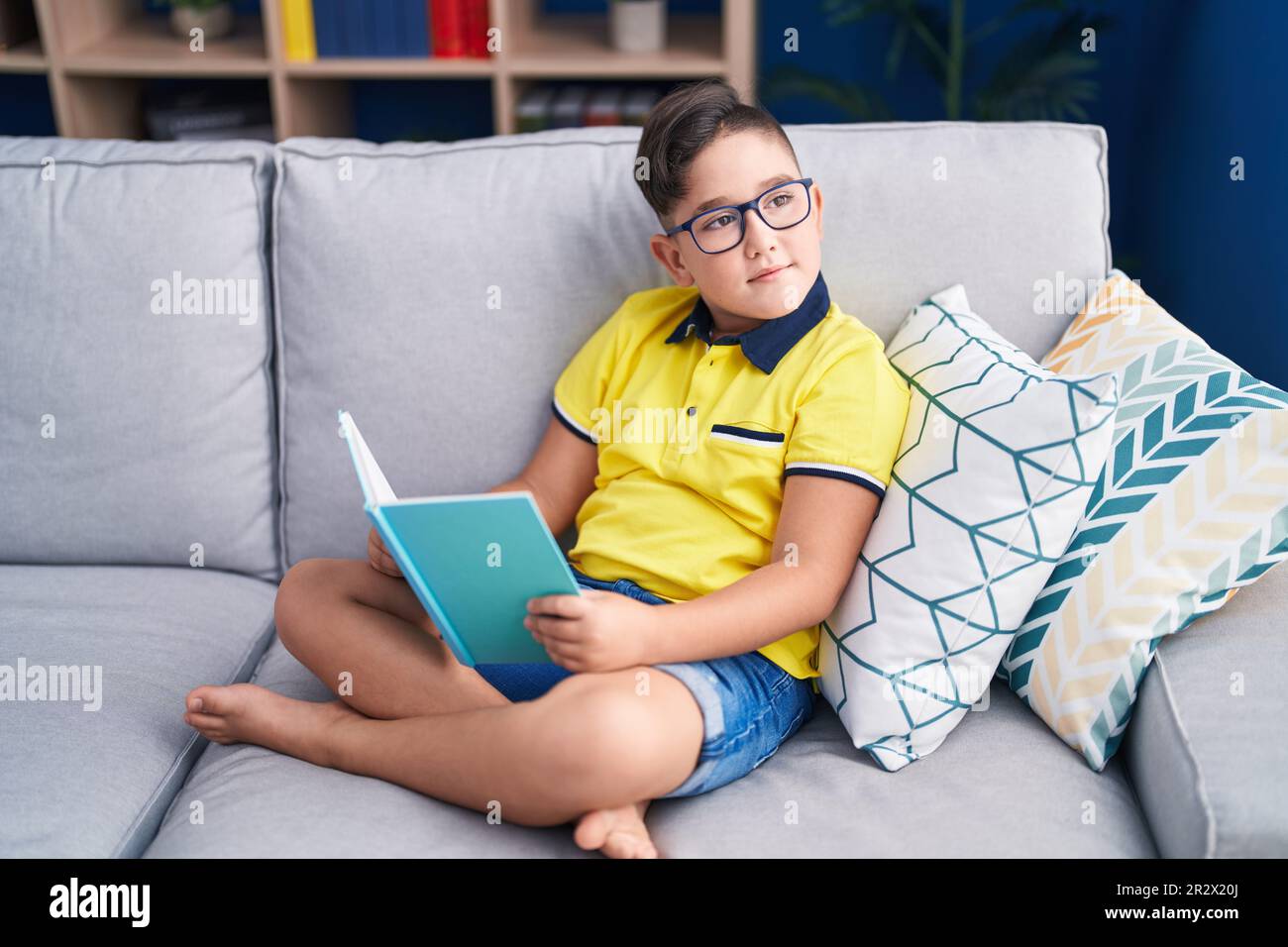 Adorable hispanic boy reading book sitting on sofa at home Stock Photo ...