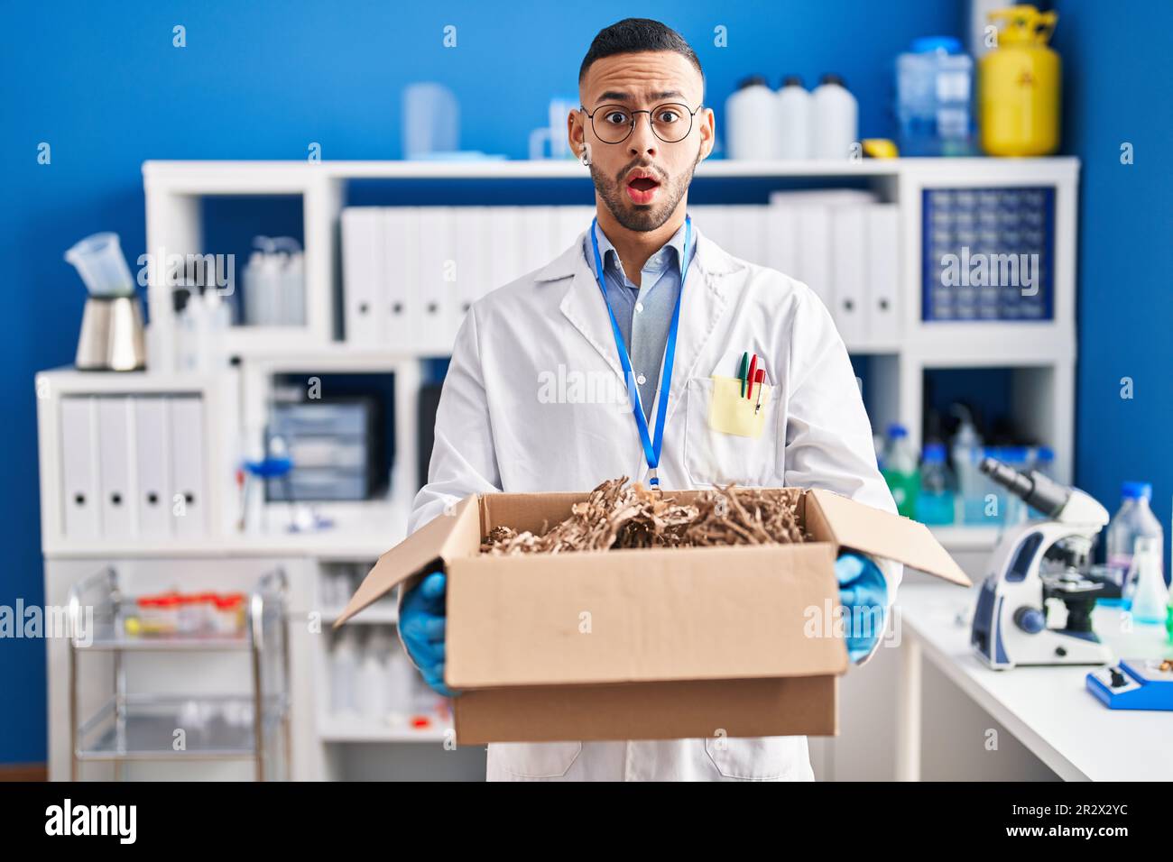 Young hispanic man working at scientist laboratory holding cardboard ...